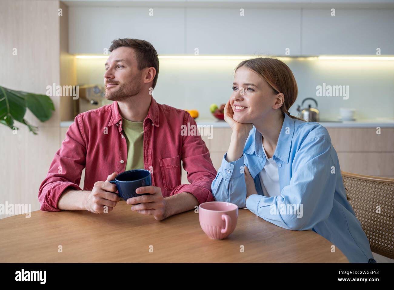 Merry couple spending weekend at home, drinking tea, looking at window, dreaming of future ...