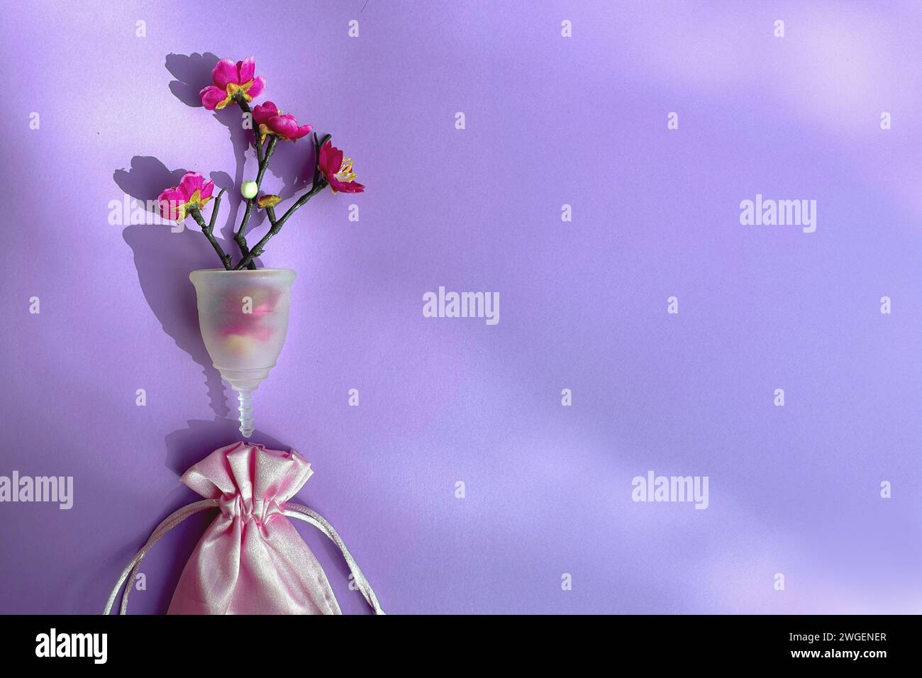 Menstrual cup with red flowers and pink silk bag, flat lay on purple ...