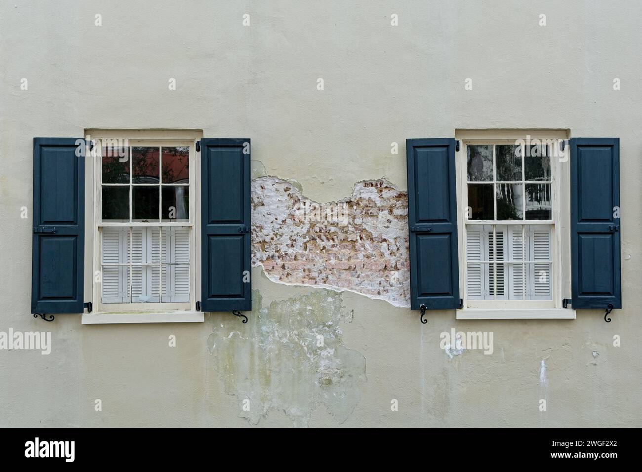 Exposed brickwork behind broken stucco between open shuttered windows ...