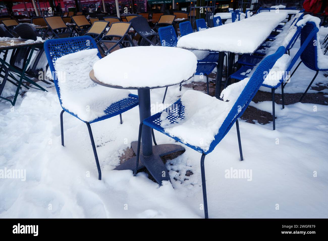 lots of snow on tables and blue chairs at tourist outdoor gastronomy in cologne's old town ...