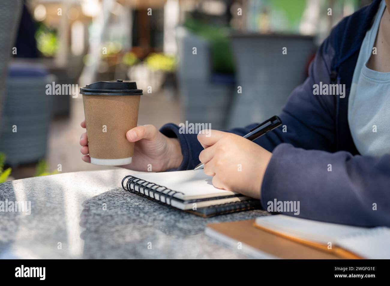 A cropped shot of a woman taking notes in a spiral notepad while ...