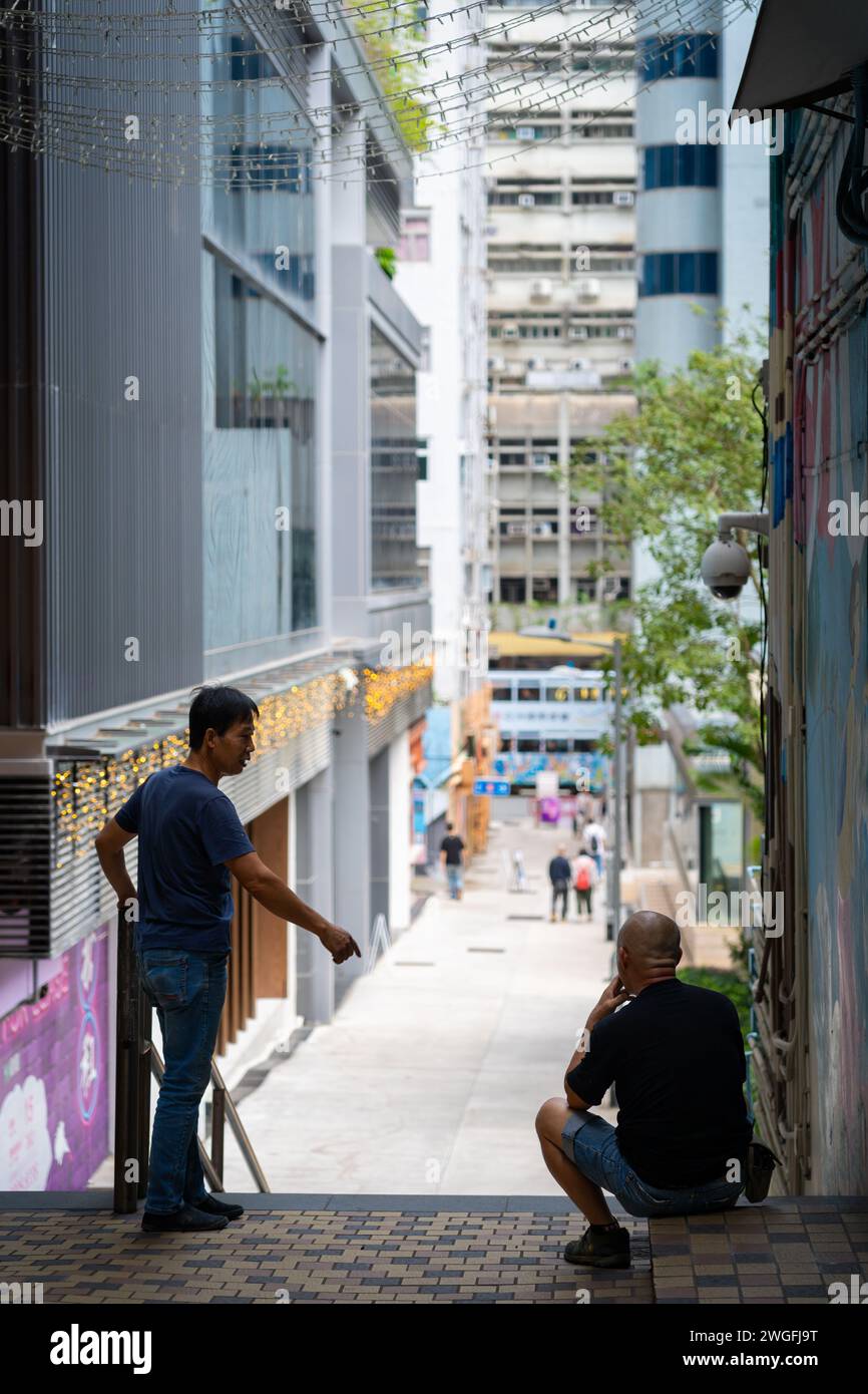 Two people seated on a sidewalk observing a standing man Stock Photo ...