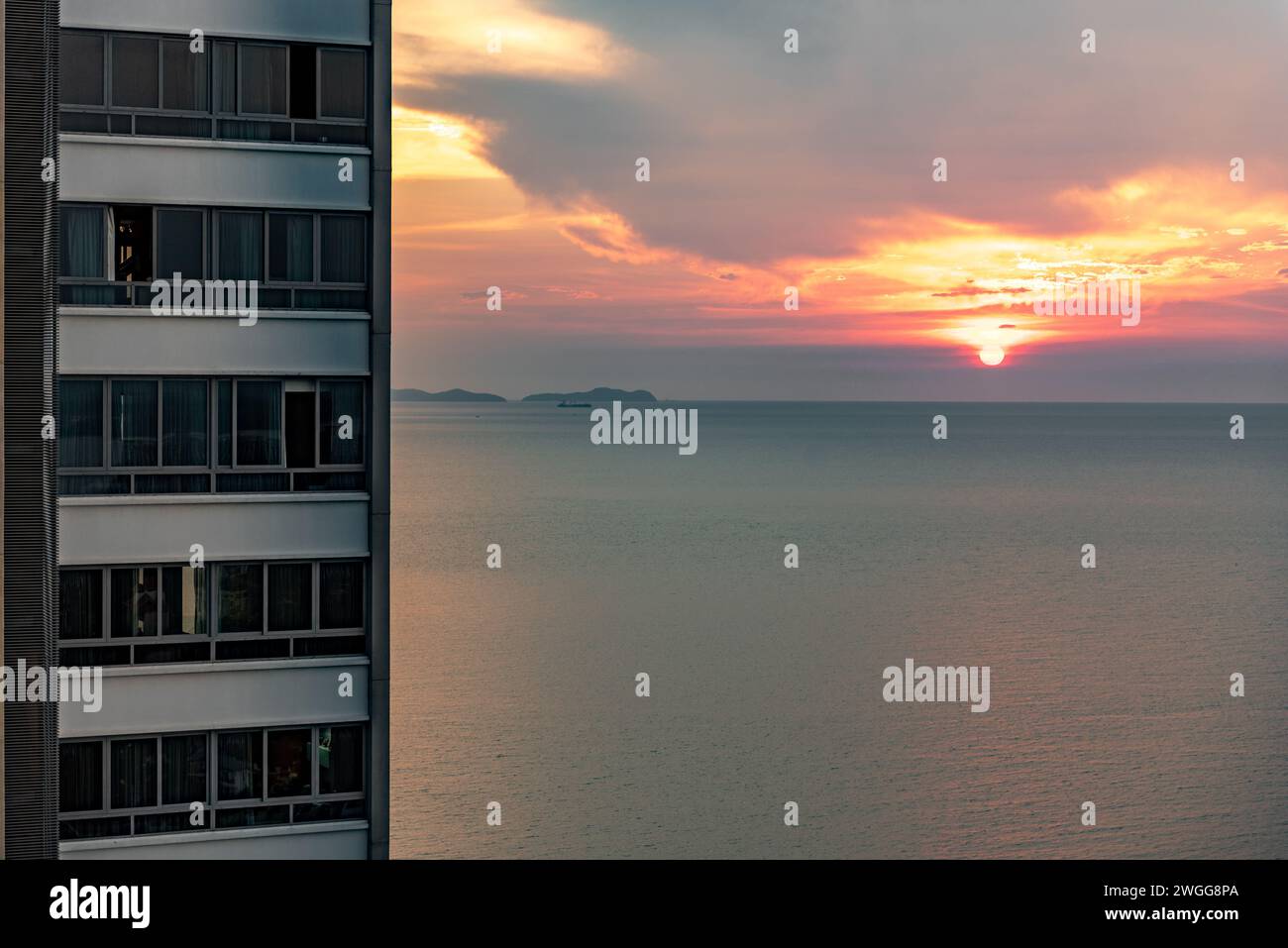 A scenic view of a sunset over the sea with a high-rise building on the ...