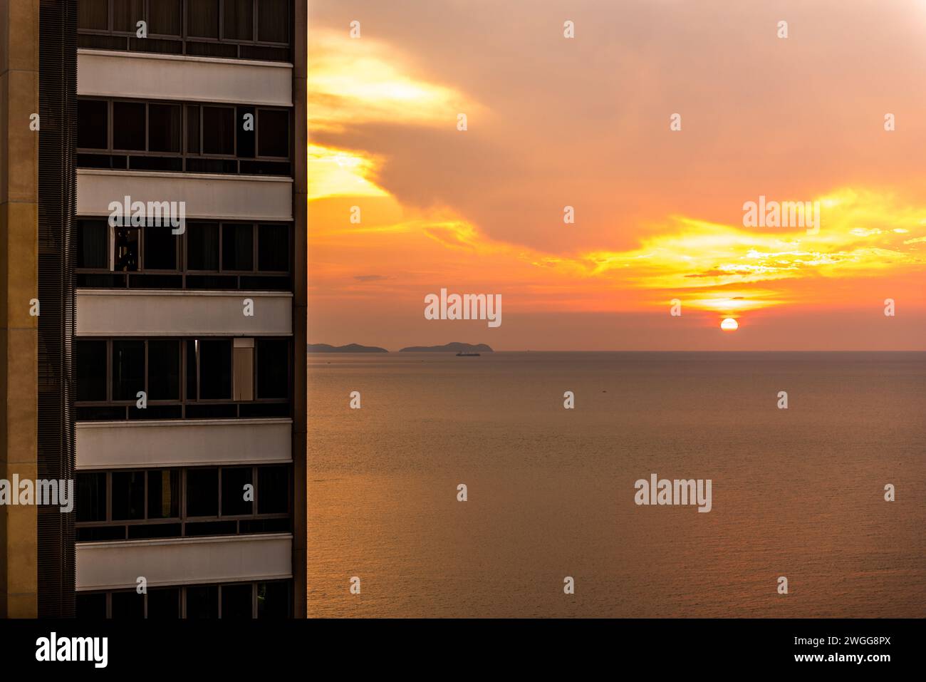 A scenic view of a sunset over the sea with a high-rise building on the ...