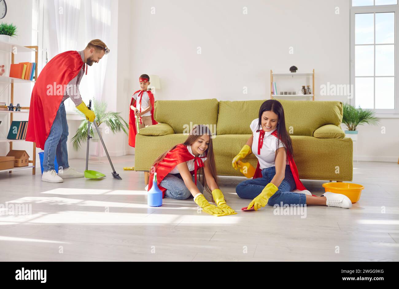 Cheerful parents and children in superhero costumes are cleaning house ...