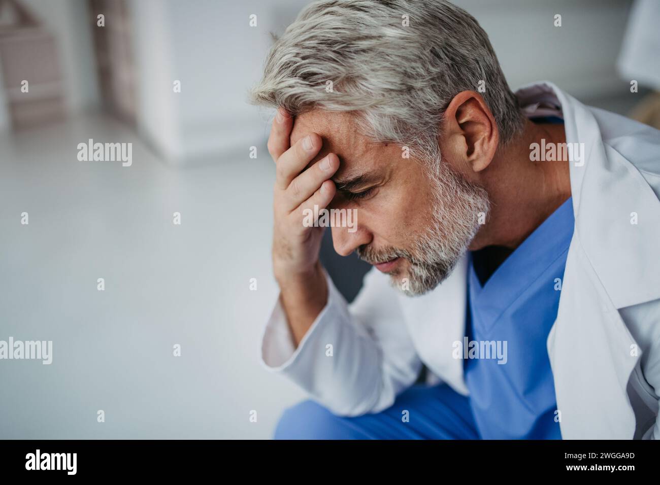 Side view of frustrated, exhausted doctor sitting in hospital corridor ...