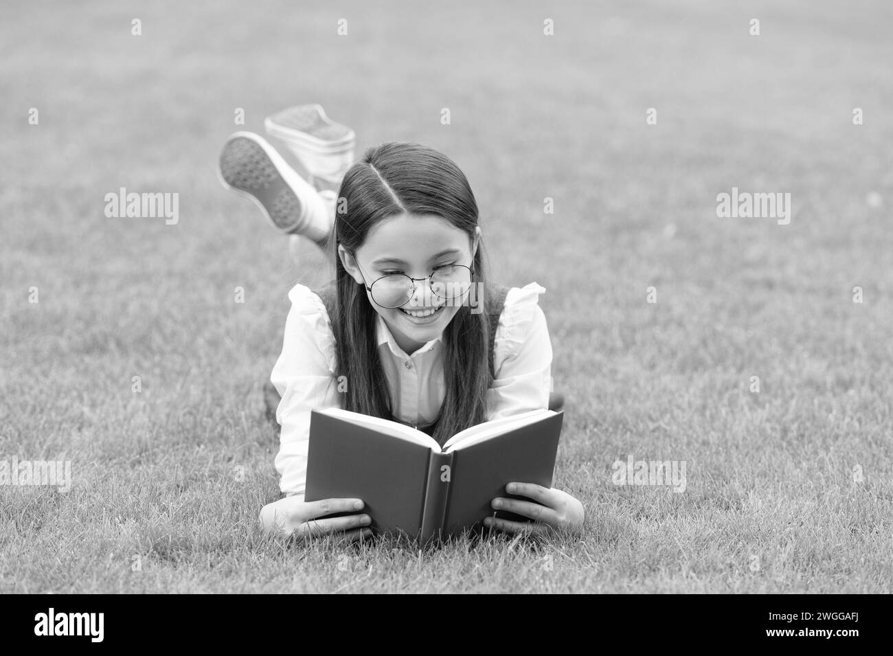 Reading time. Happy teen girl reading book lying on grass after school ...