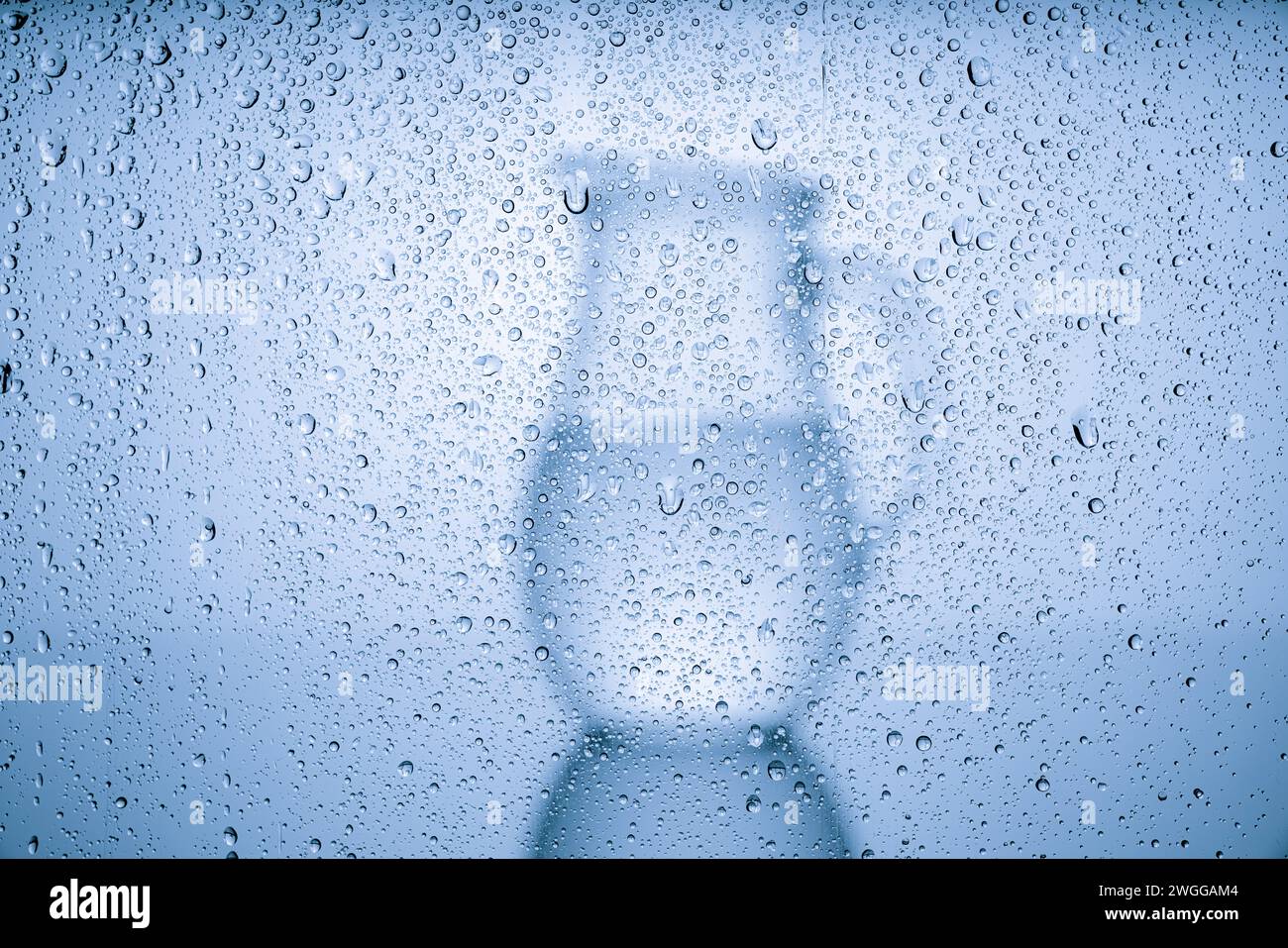 silhouette of a jug of water behind glass covered with water drops ...