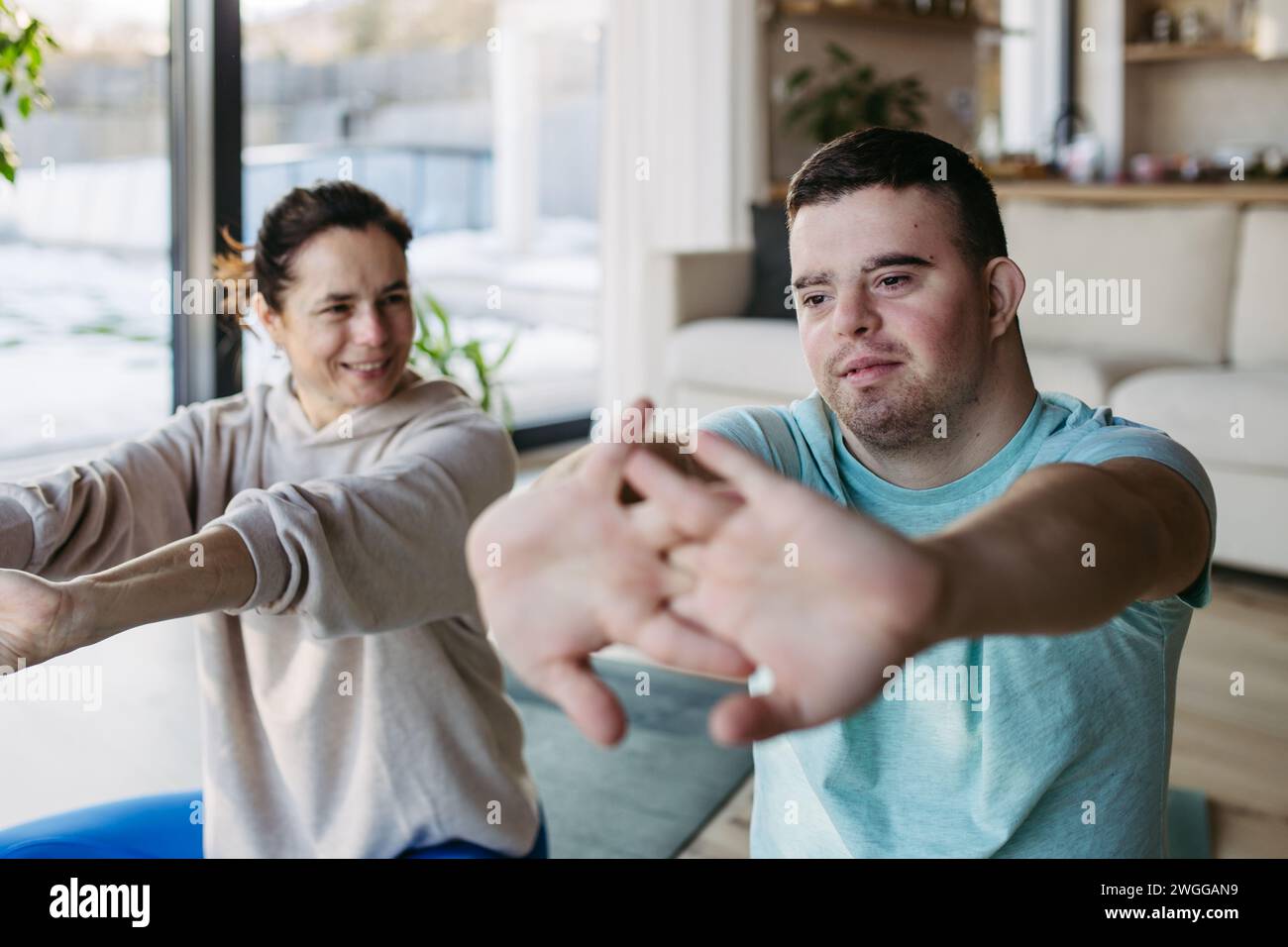 Young man with Down syndrome exercising at home with his mother on ...