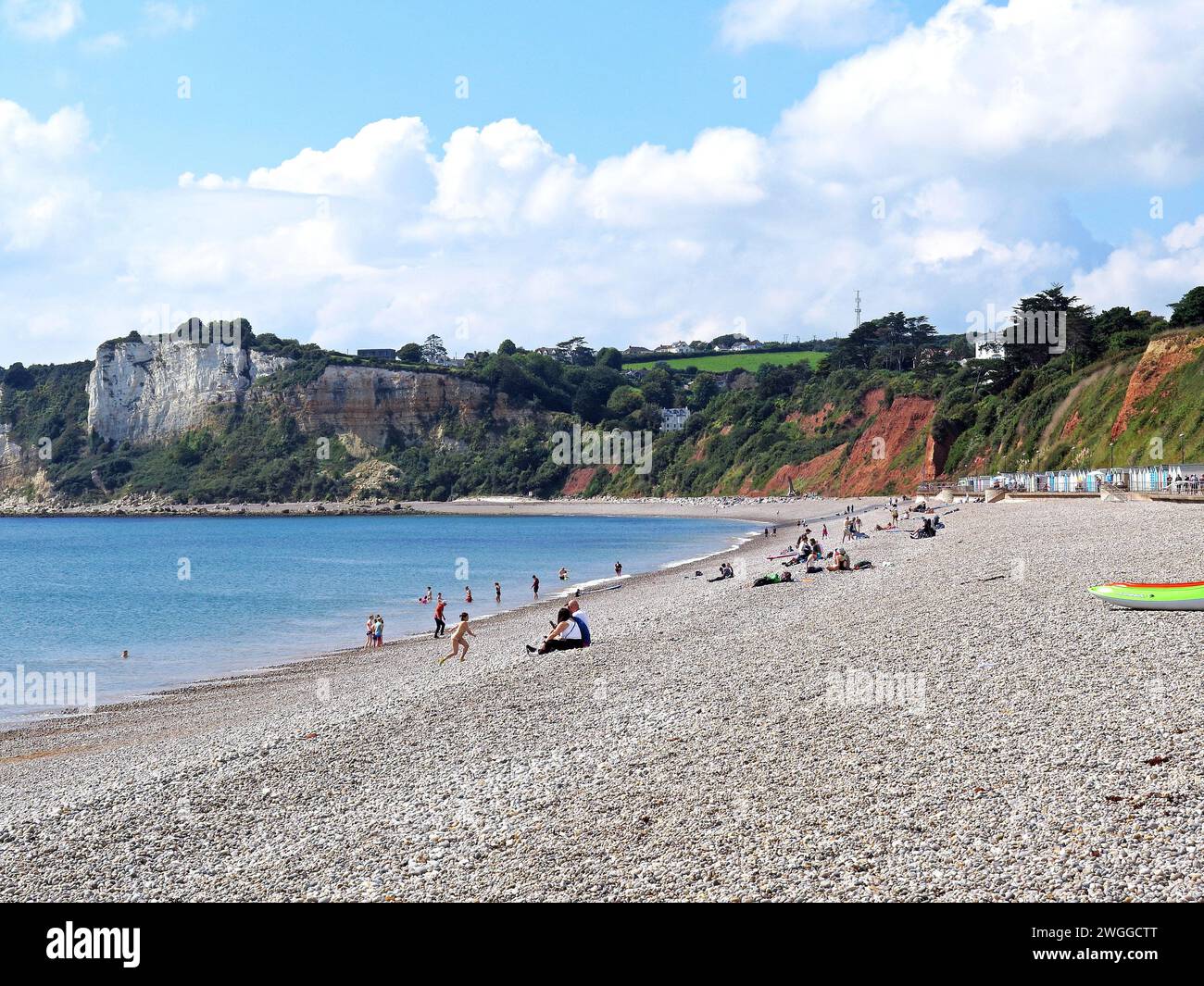Tourists relaxing on the pebble beach with Jurassic cliffs to the rear ...