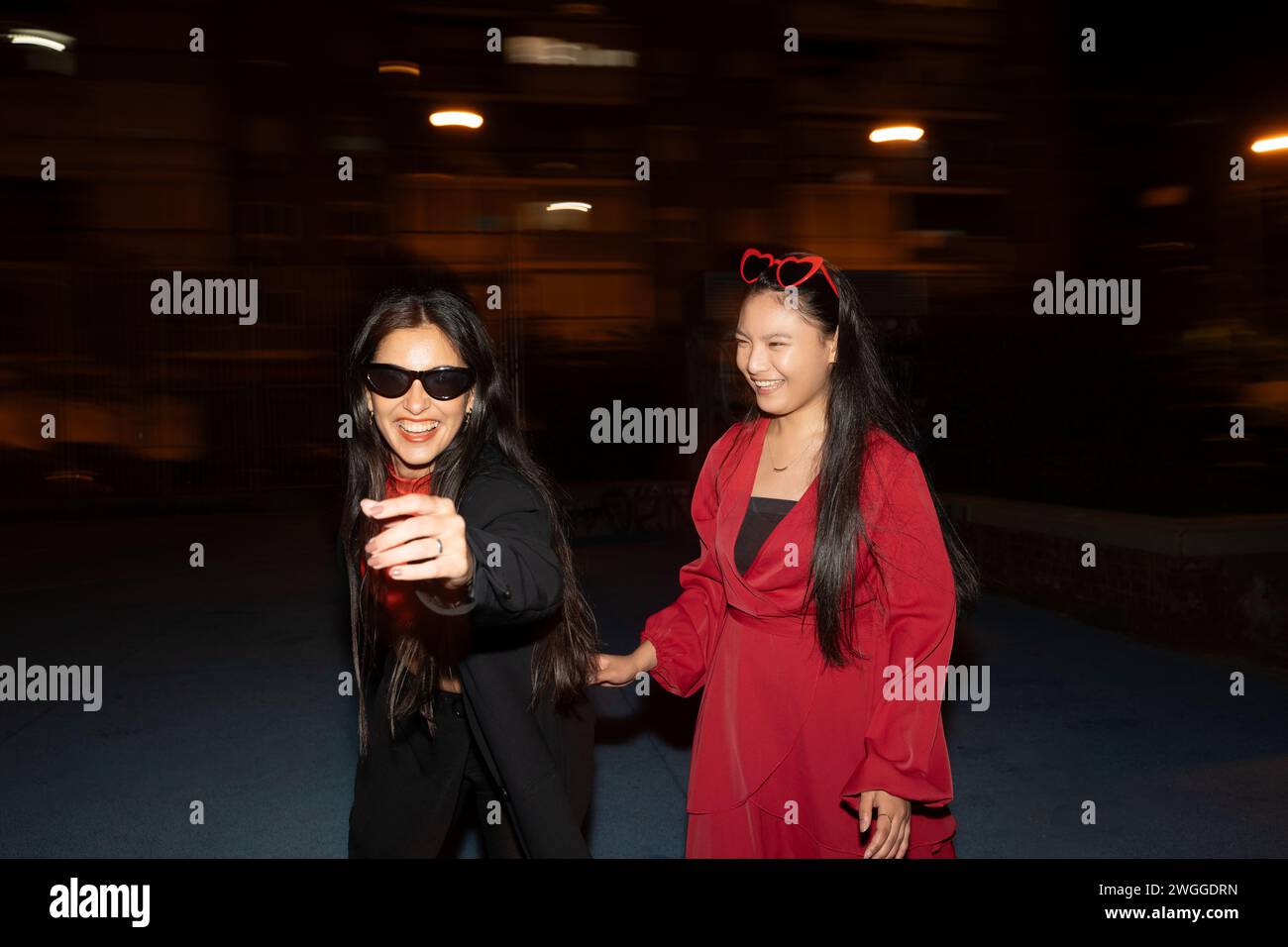 Two delighted women dance on an urban street at night, their smiles ...