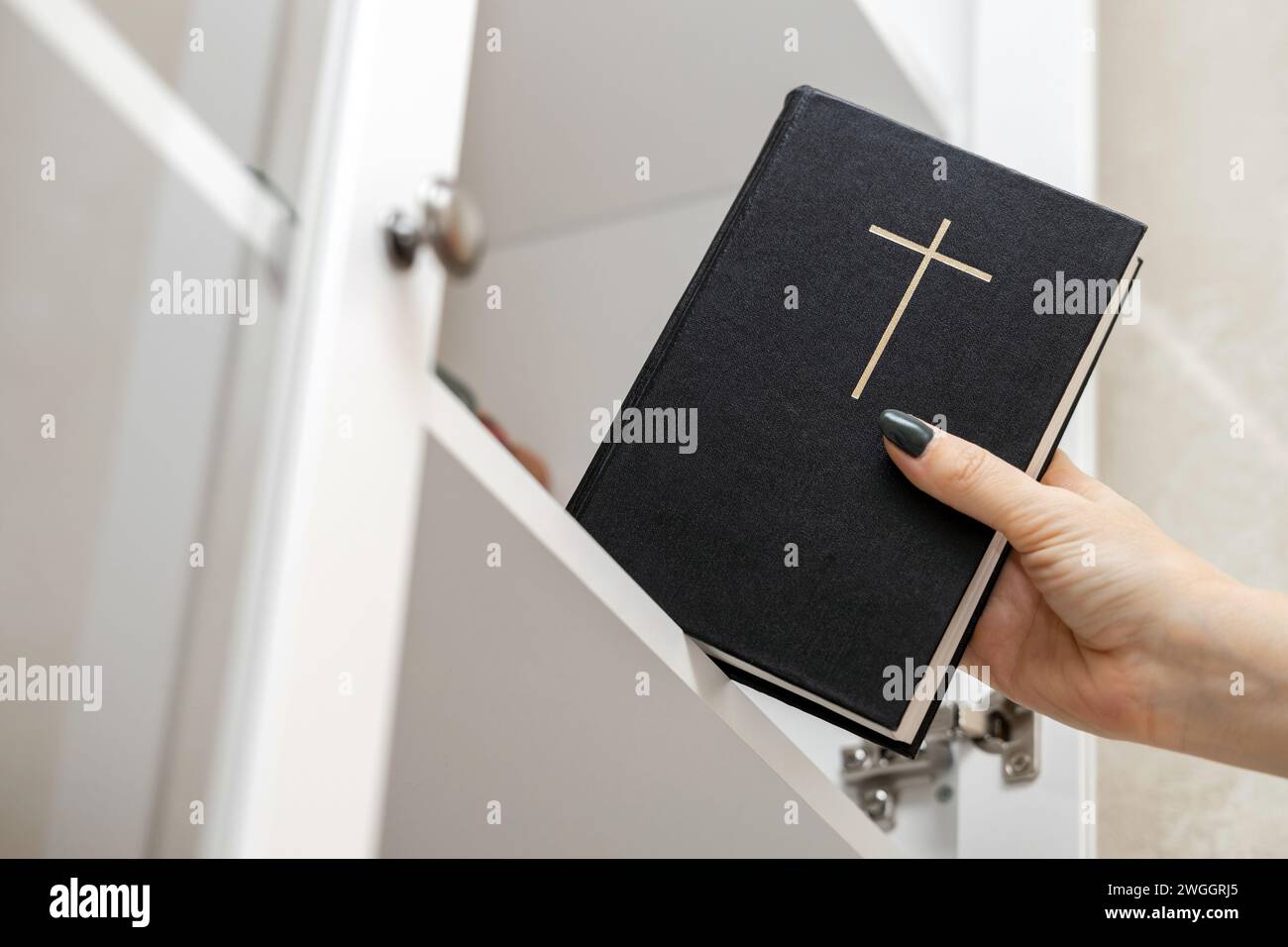woman takes out a bible from a bookcase. hand removes bible from ...