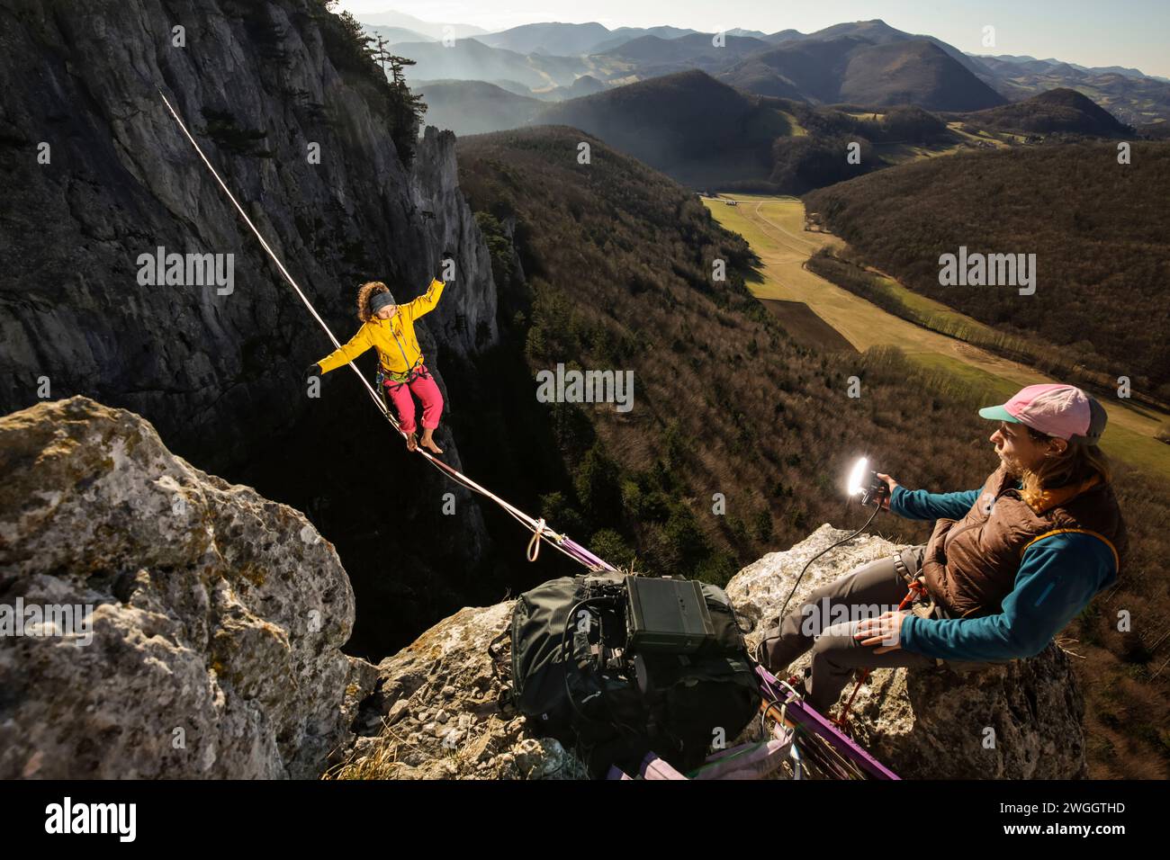 A photographer holds a light up to a highline athlete walking on ...