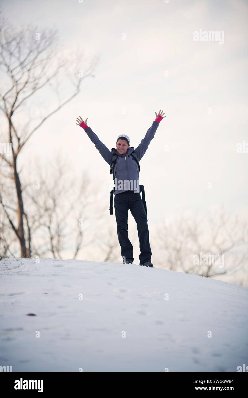 A young woman raises her arms in celebration while on a winter hike ...