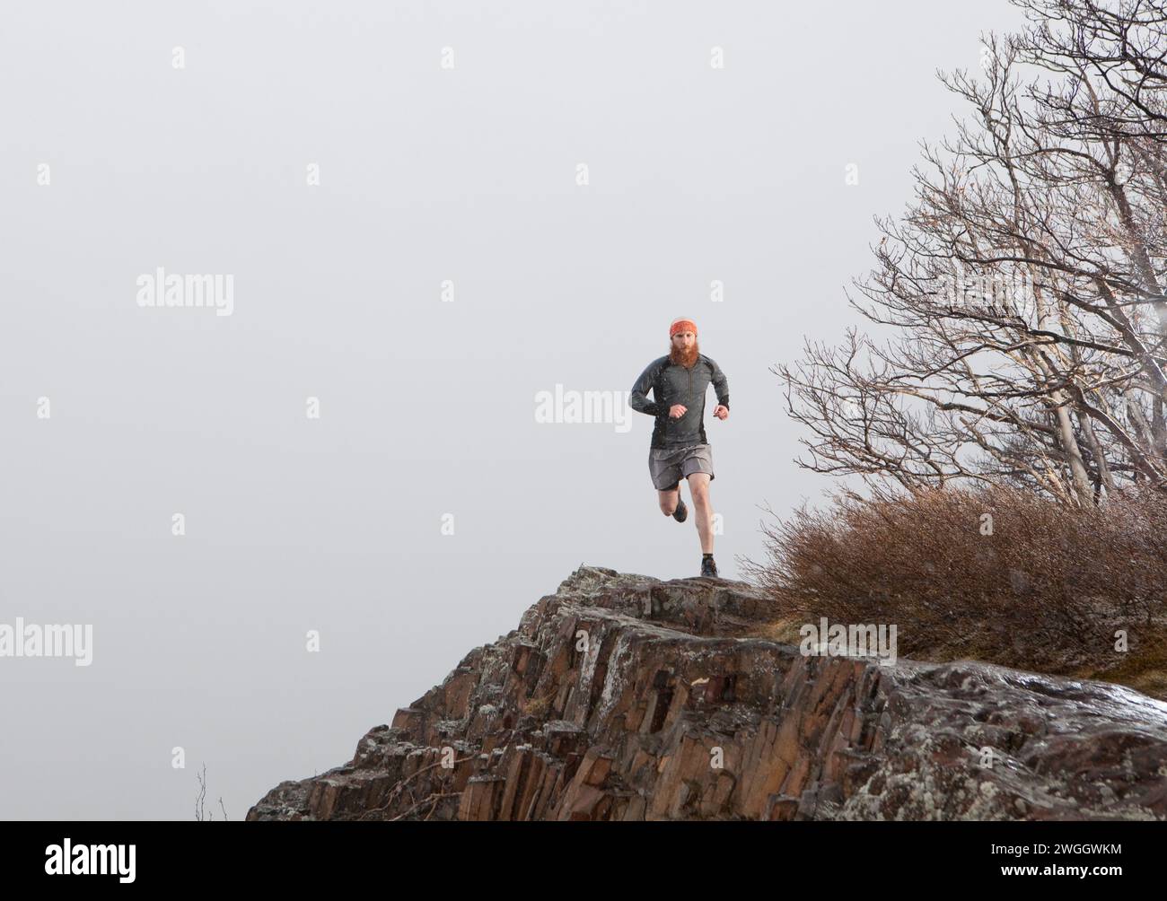 A trail male trail runner traverses a cliff face in the fog and snow ...