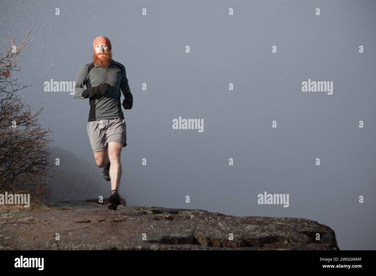 A trail runner with a long beard runs along the edge of a cliff in the ...