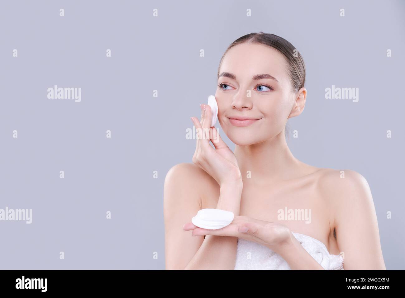 Beautiful woman cleaning her face with cotton swab over background and ...