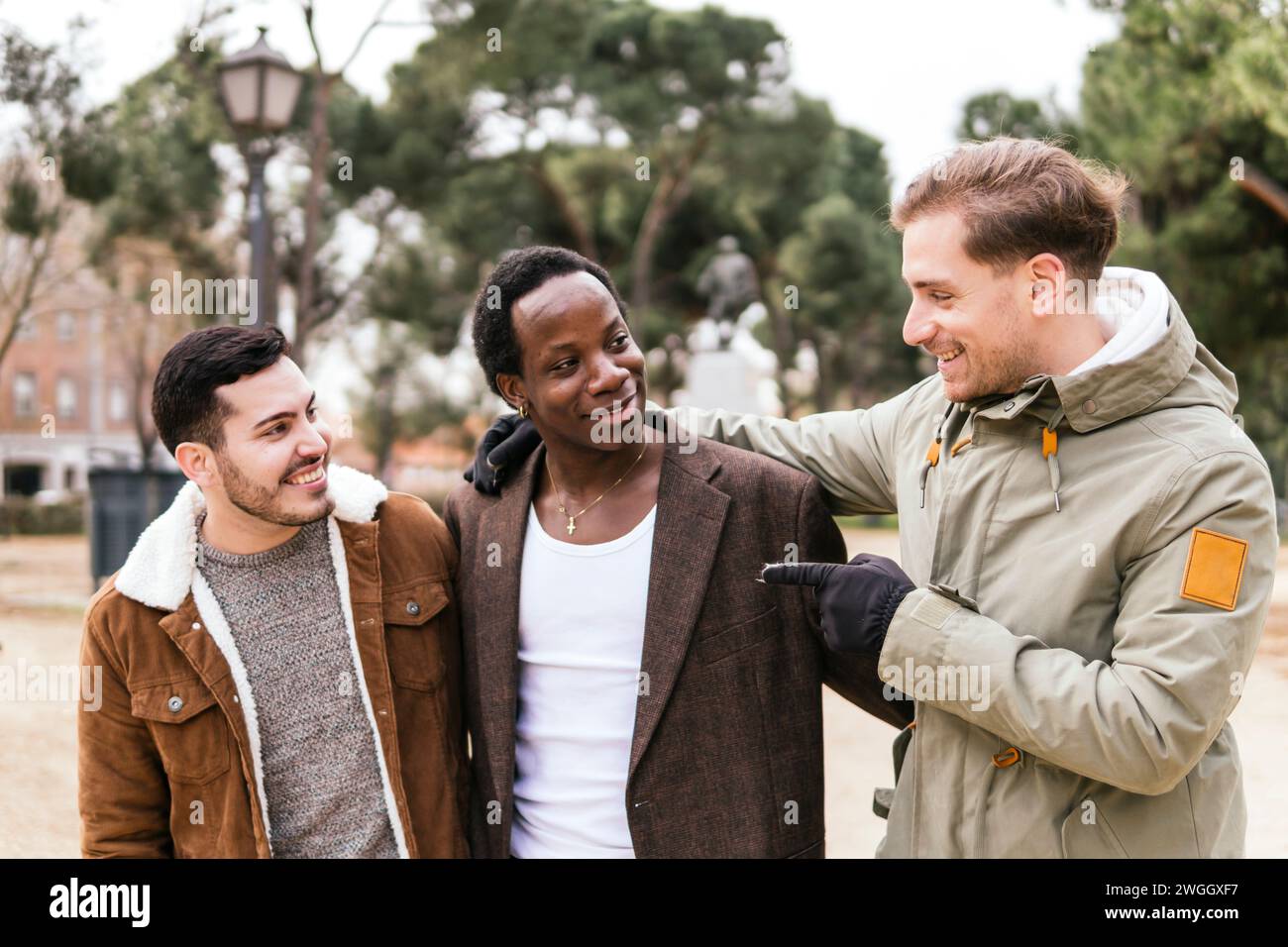 three multiracial friends speaking down around trees Stock Photo - Alamy