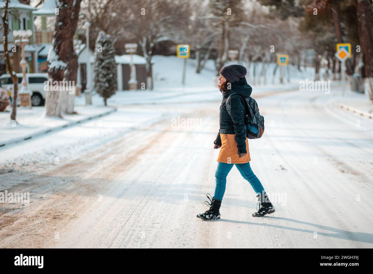 A young woman in a jacket and hat crosses a snow-covered empty street. Side view Stock Photo - Alamy