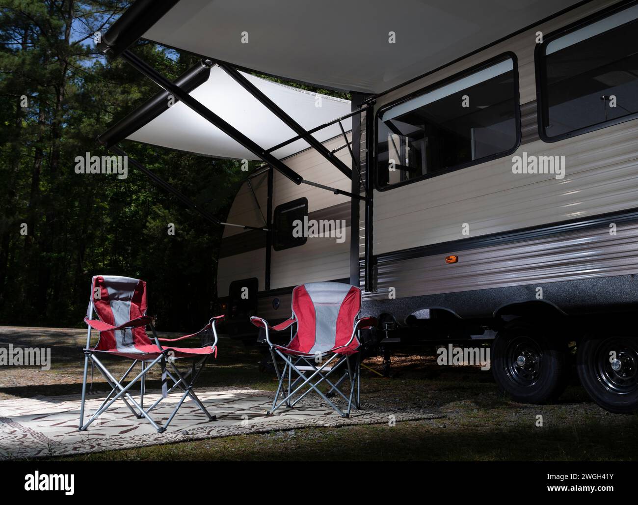 Forested campsite with a travel trailer set up with two awnings out and ...