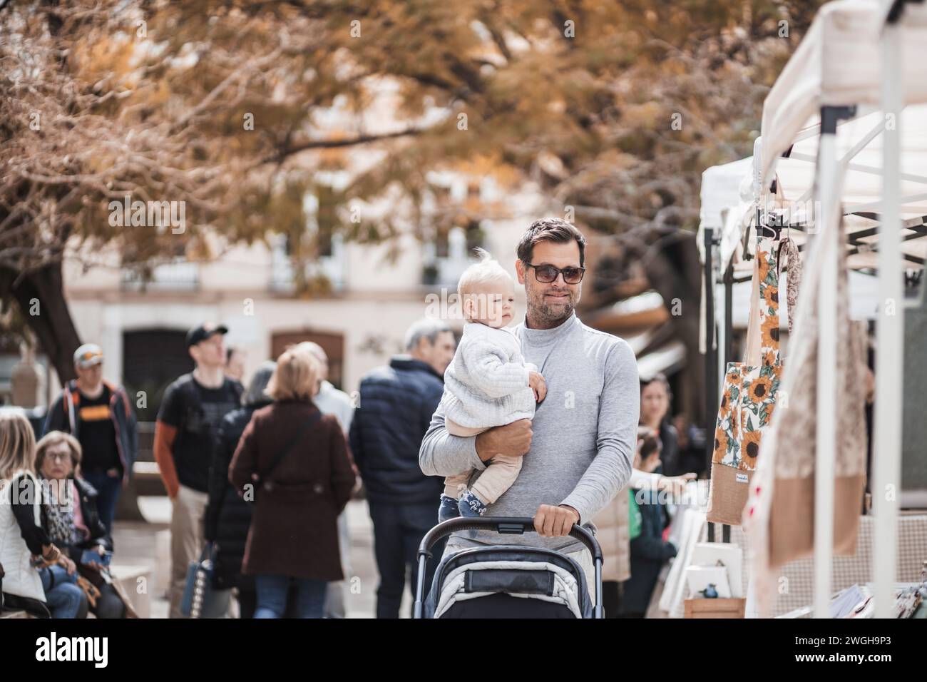 Father walking carrying his infant baby boy child and pushing stroller ...