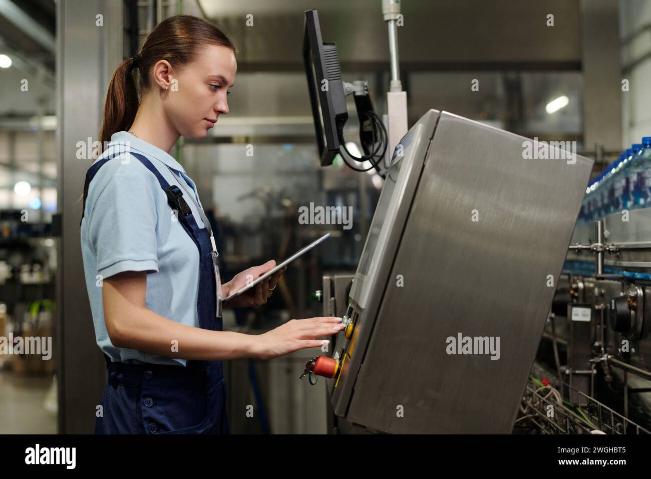 Young worker of plant standing in front of factory equipment and ...