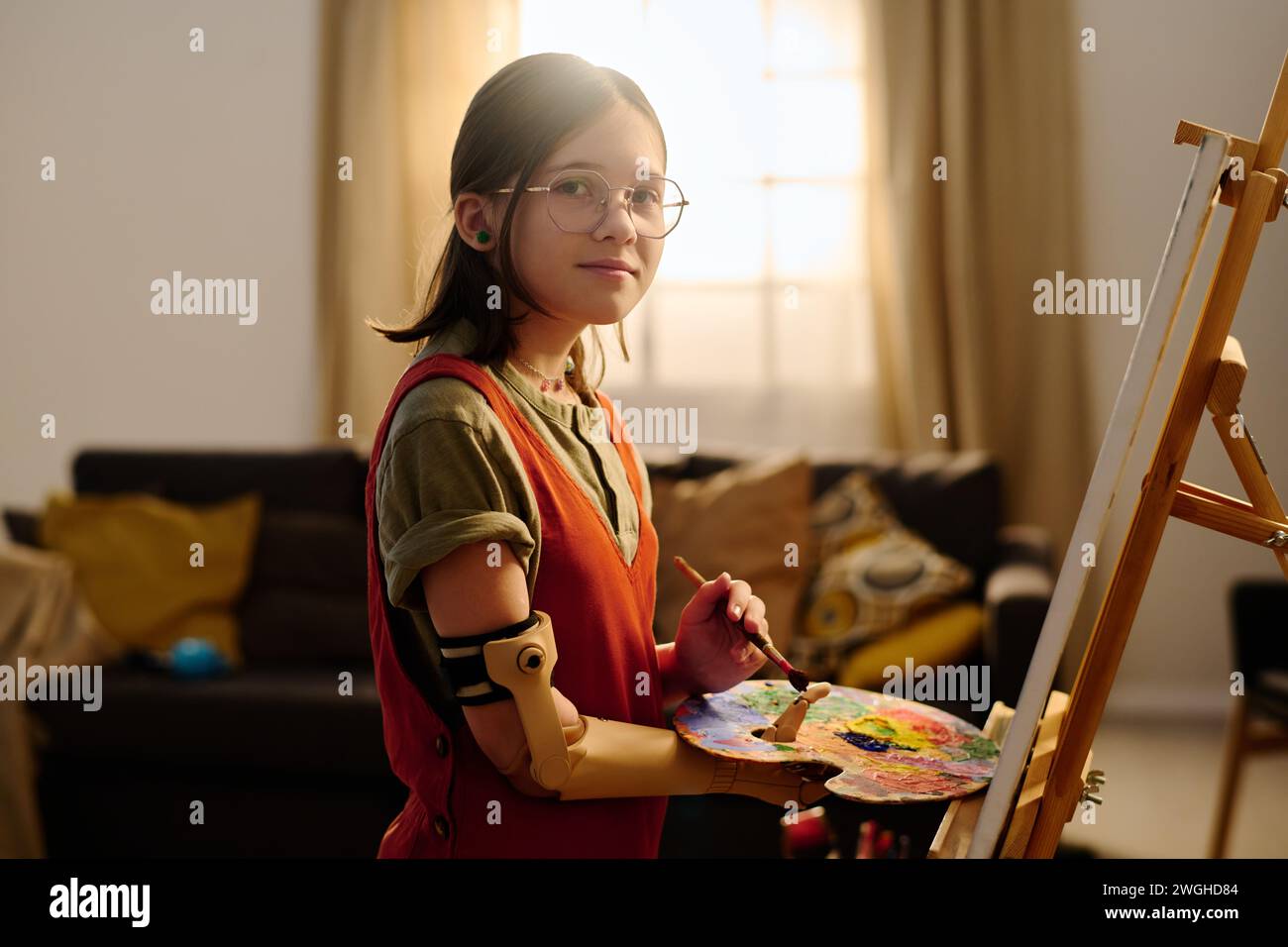 Pre-teen girl with disability looking at camera while standing in front ...