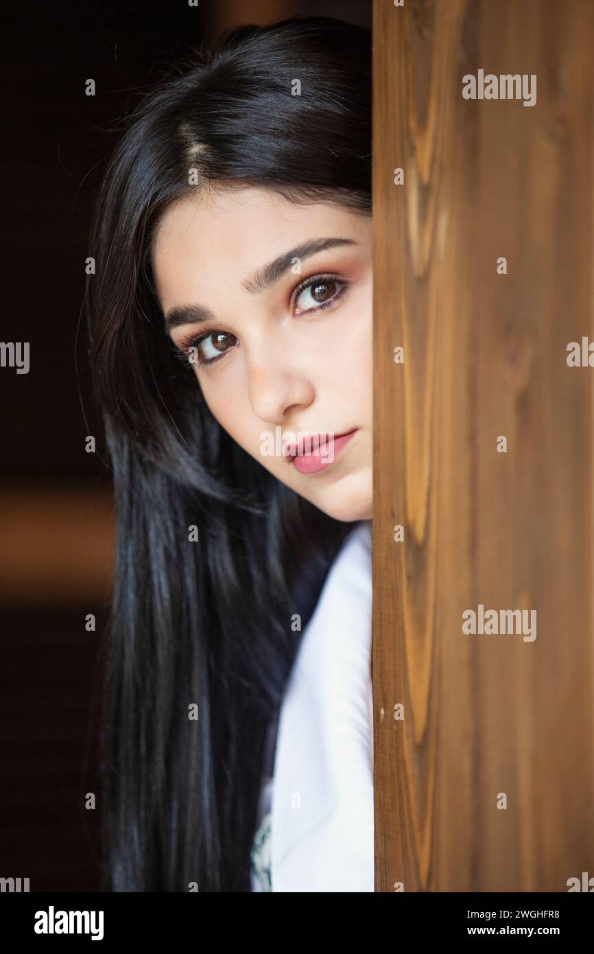 Beautiful woman hiding behind door looking at camera Stock Photo - Alamy