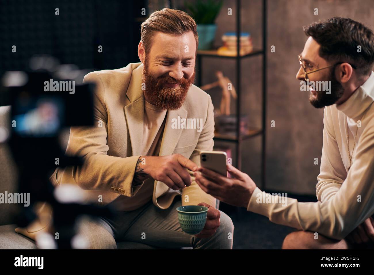 two cheerful elegant men with beards in chic clothes looking at ...