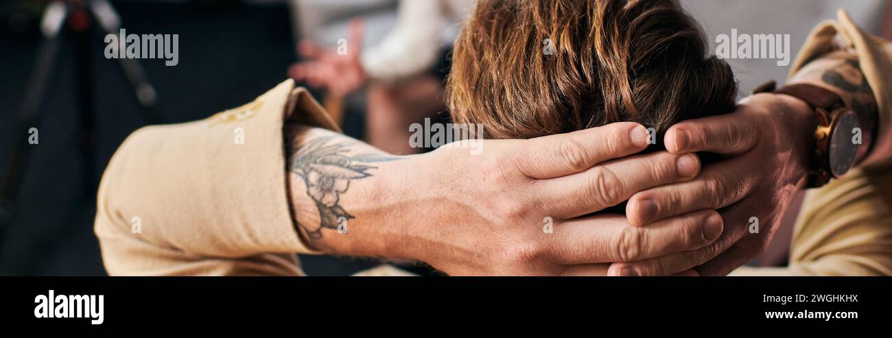 focus on man posing with hands behind his head next to his blurred ...