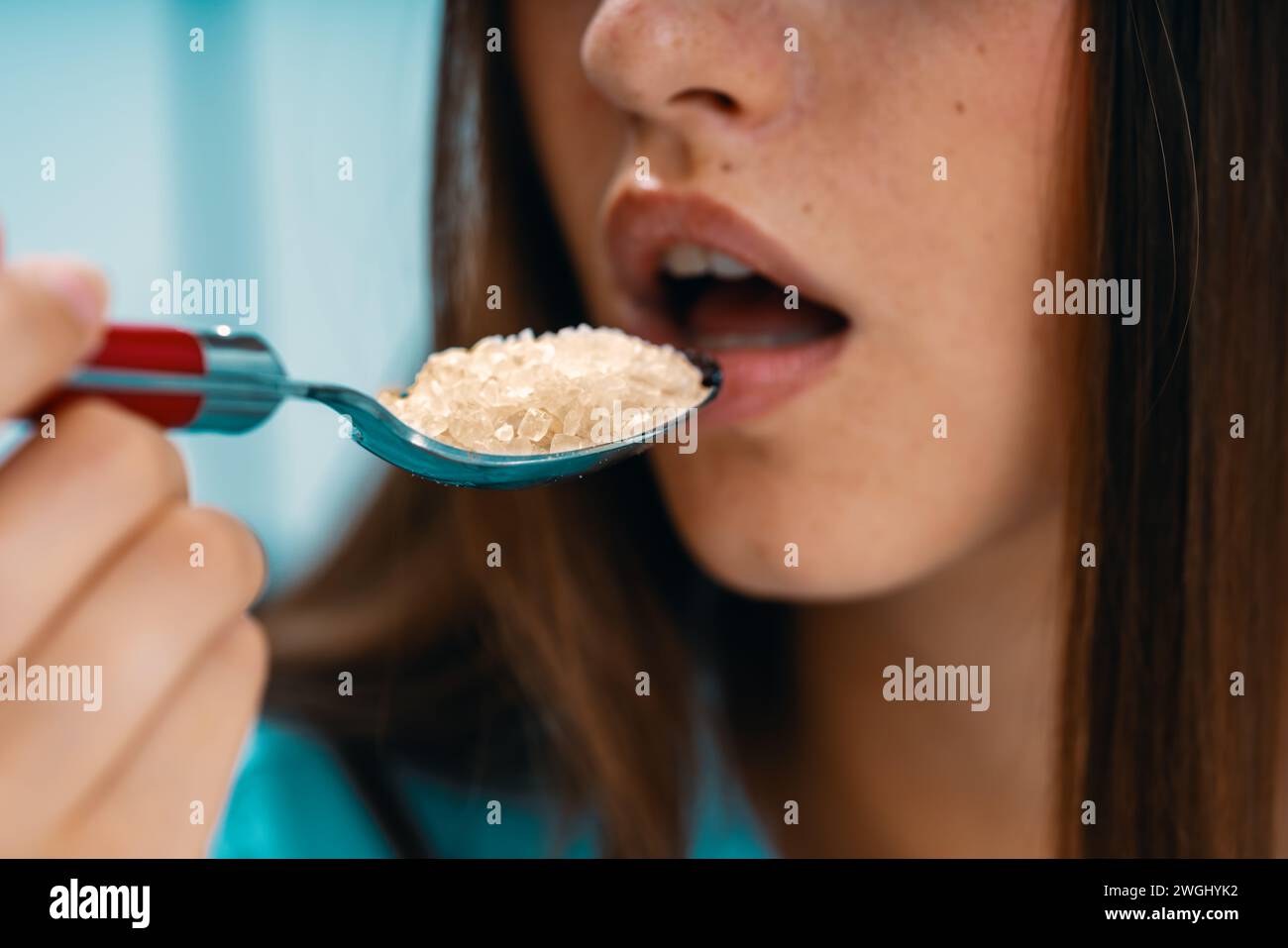 young woman putting a spoonful of sugar in her mouth, unhealthy food ...