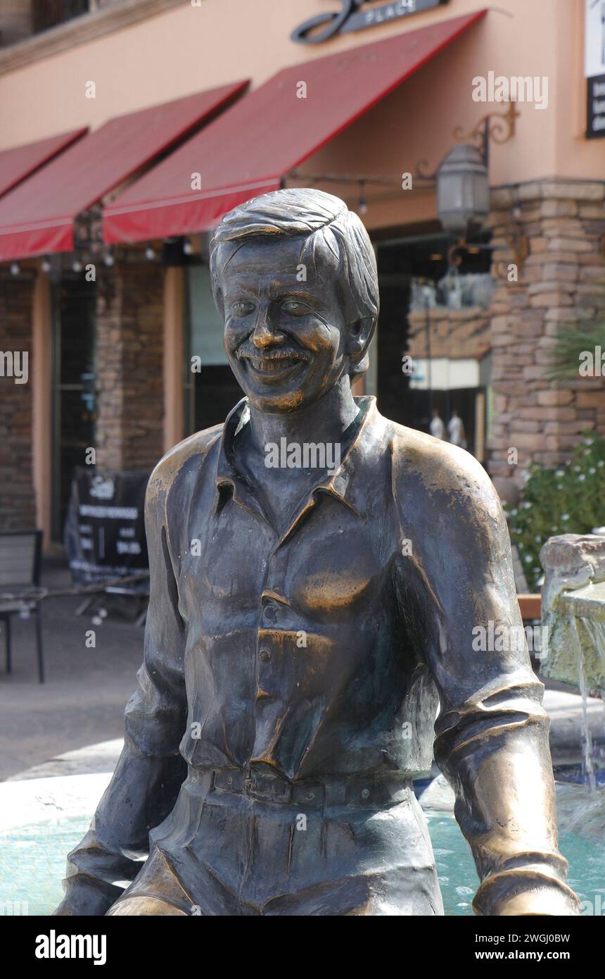 A bronze statue of a man, smiling and wearing a collared shirt with ...