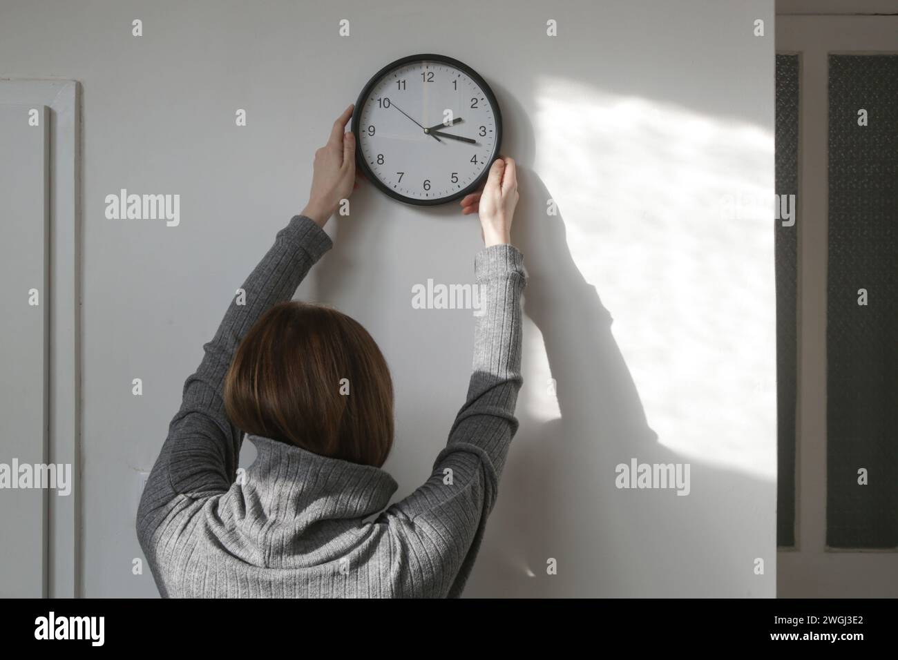Young woman hanging clock on the wall, back view Stock Photo - Alamy