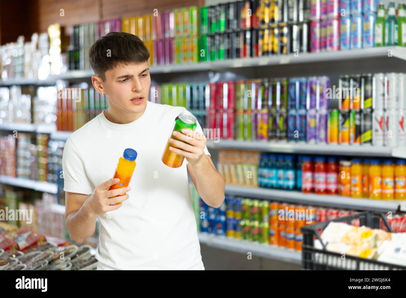Young guy choosing colored drinks in drinks section of supermarket ...