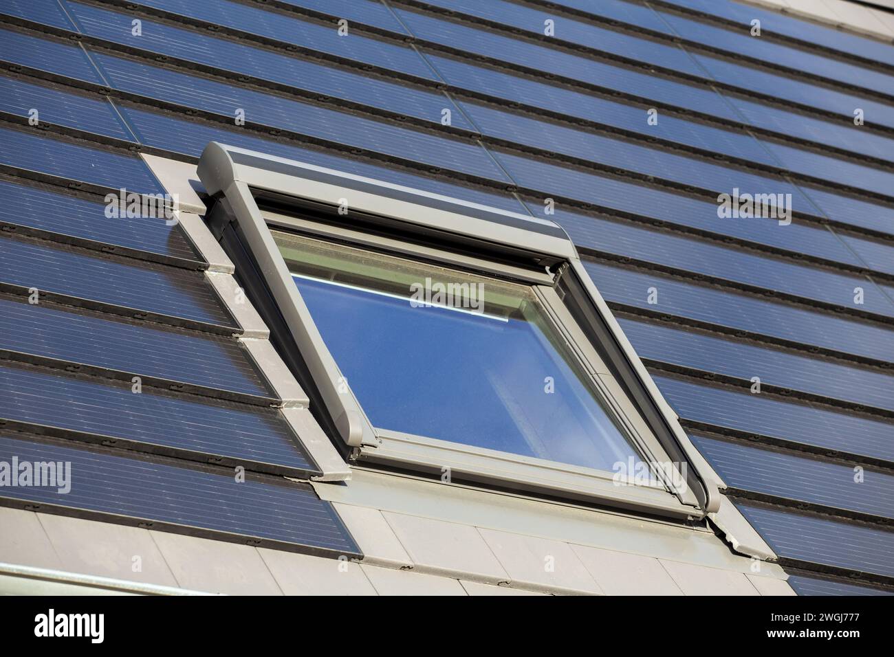 Roof window on a detached house with solar roof tiles. Solar tiles are ...