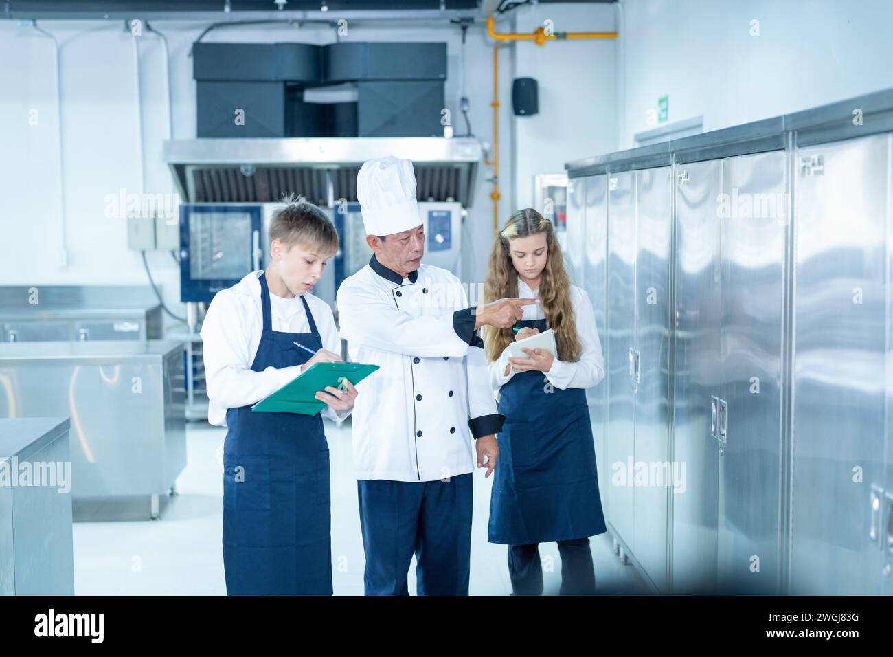 Senior male chef teaches young teenage boys cooking in school kitchen ...