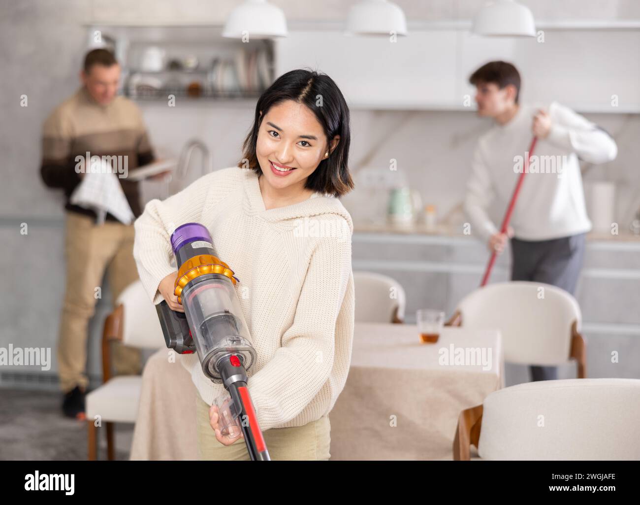 Girl vacuuming floor while his relatives help tidy up room Stock Photo ...
