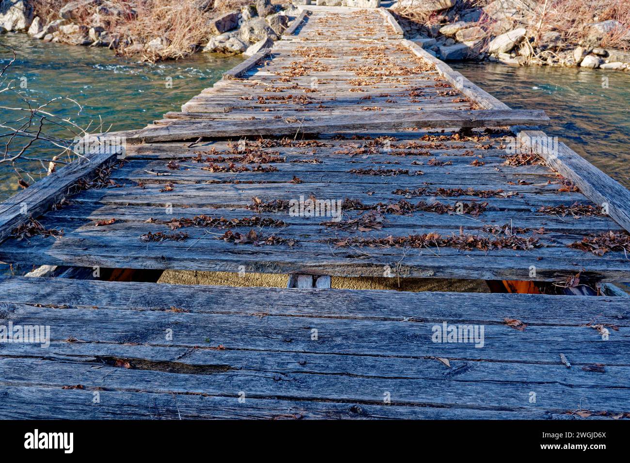 A weathered old wooden bridge for vehicle crossing over a wide creek is ...
