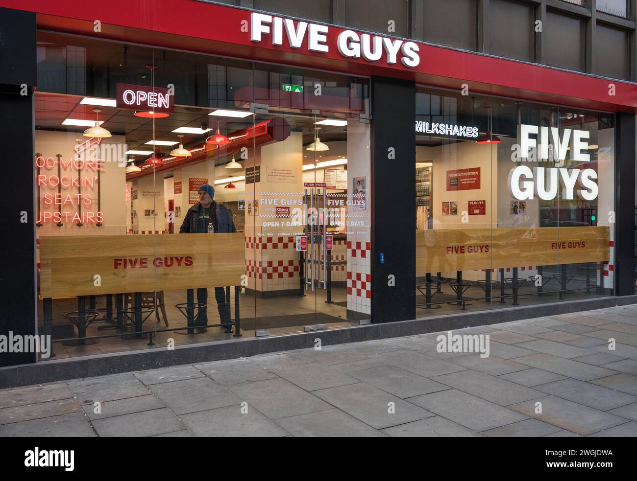 Exterior of Five Guys Hamburger restaurant. Lone man stands inside ...