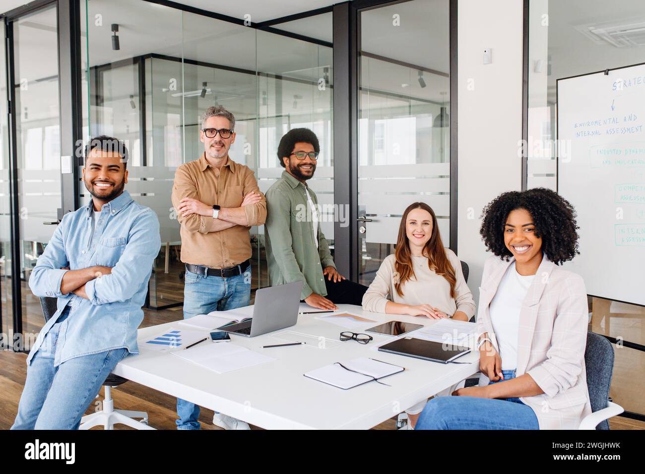 A diverse group of five colleagues beams with pride in their office ...