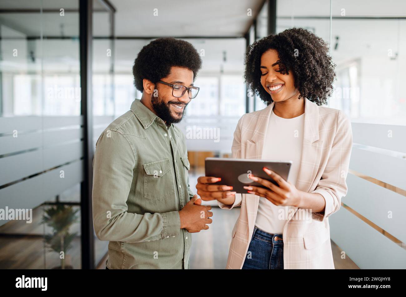 Two cheerful colleagues are sharing a tablet screen, the woman pointing ...
