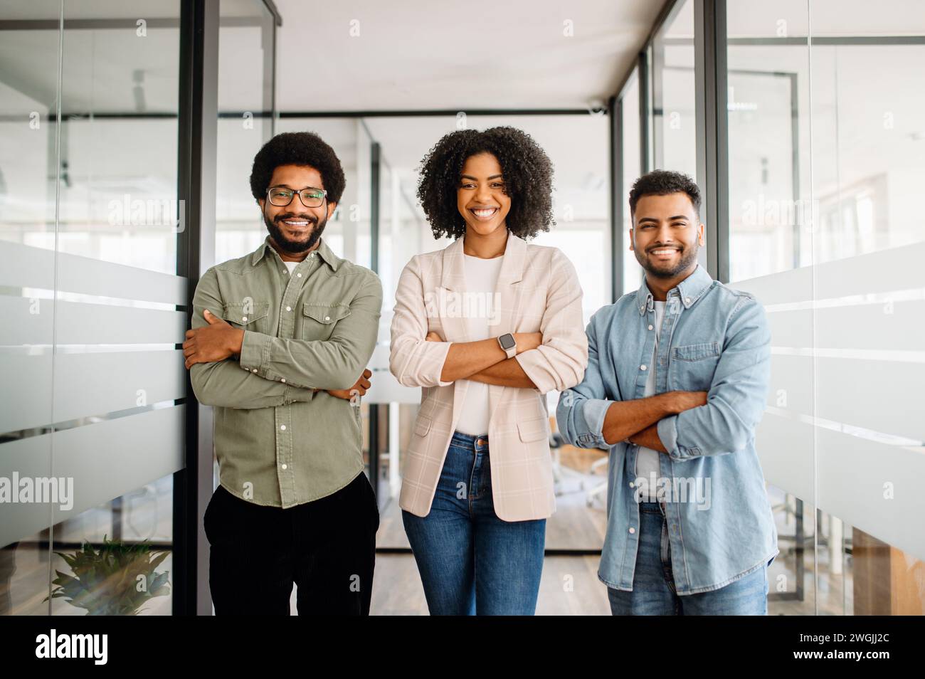Three vibrant colleagues stand together in an office, their arms ...