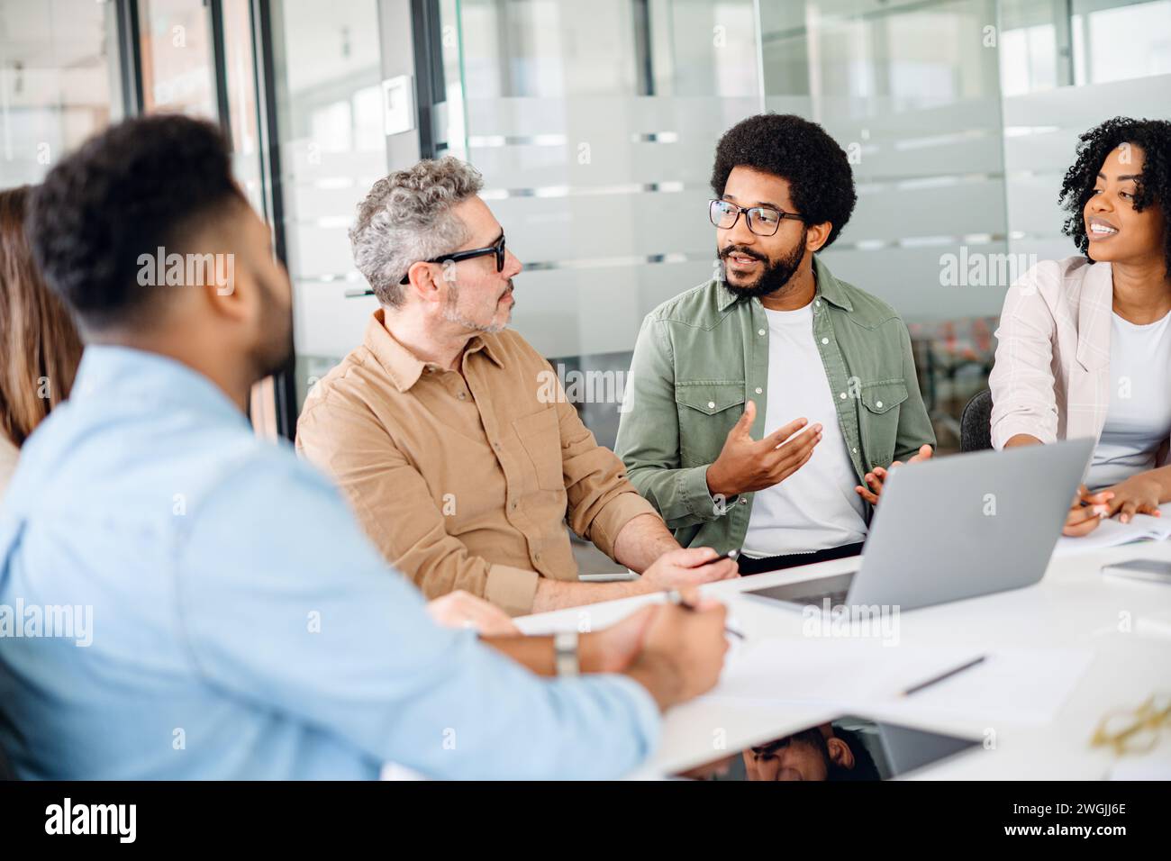 Colleagues converse around a laptop, with one member explaining a ...