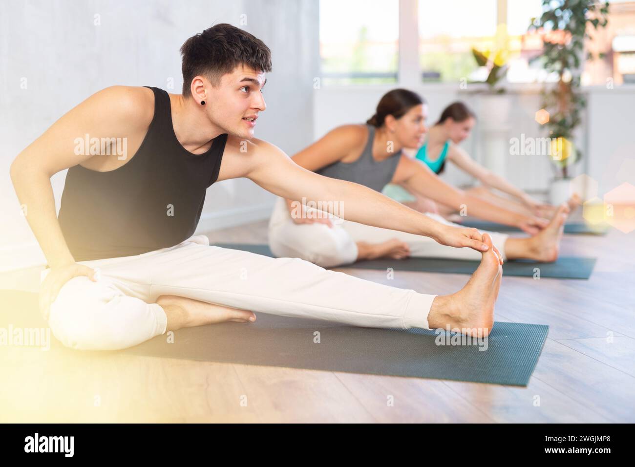 Young people doing one leg forward bend pose in class Stock Photo - Alamy