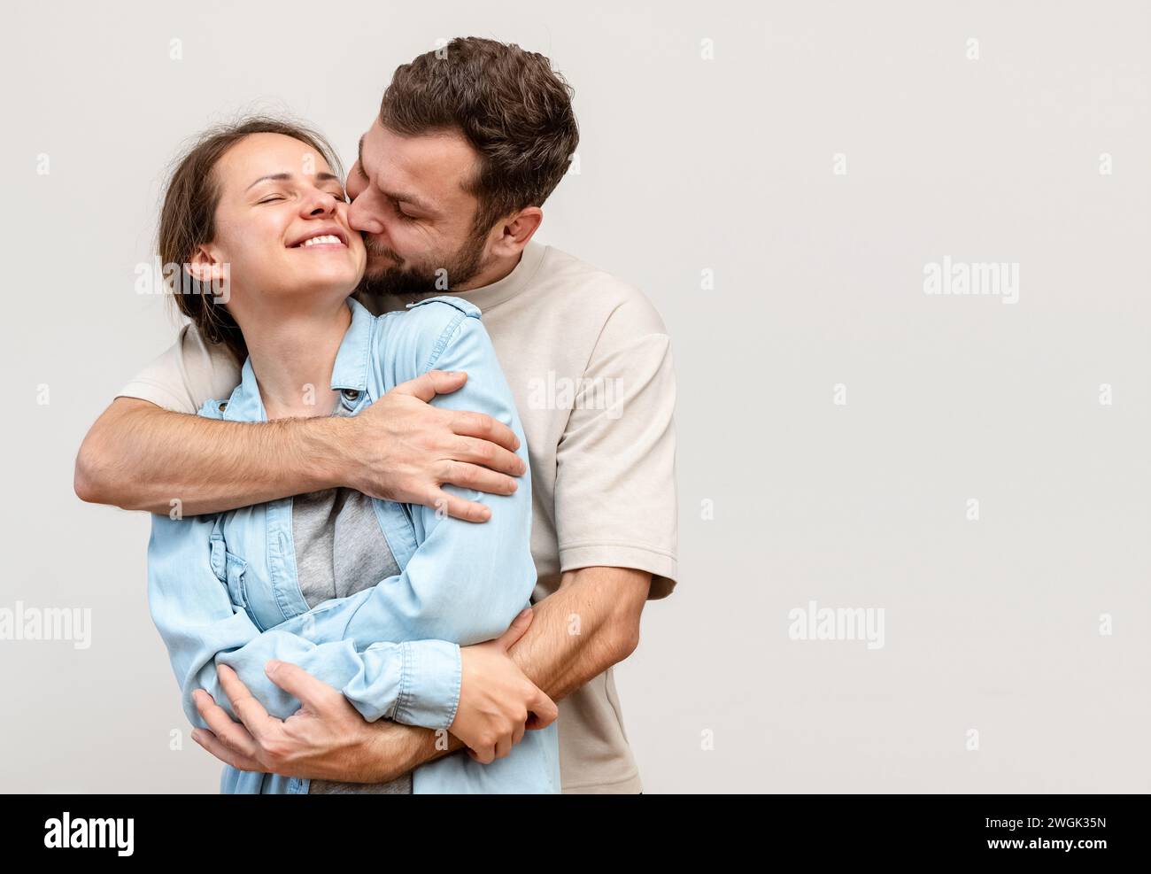 Happy young woman in the arms of her husband in front of light grey ...