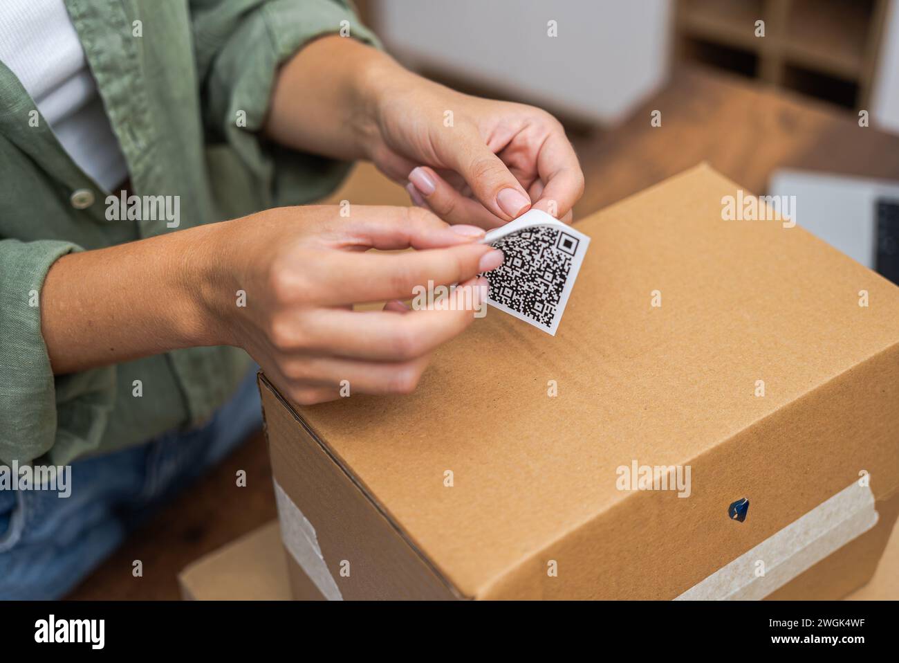 close up woman attaches qr code sticker to cardboard parcel to return ...