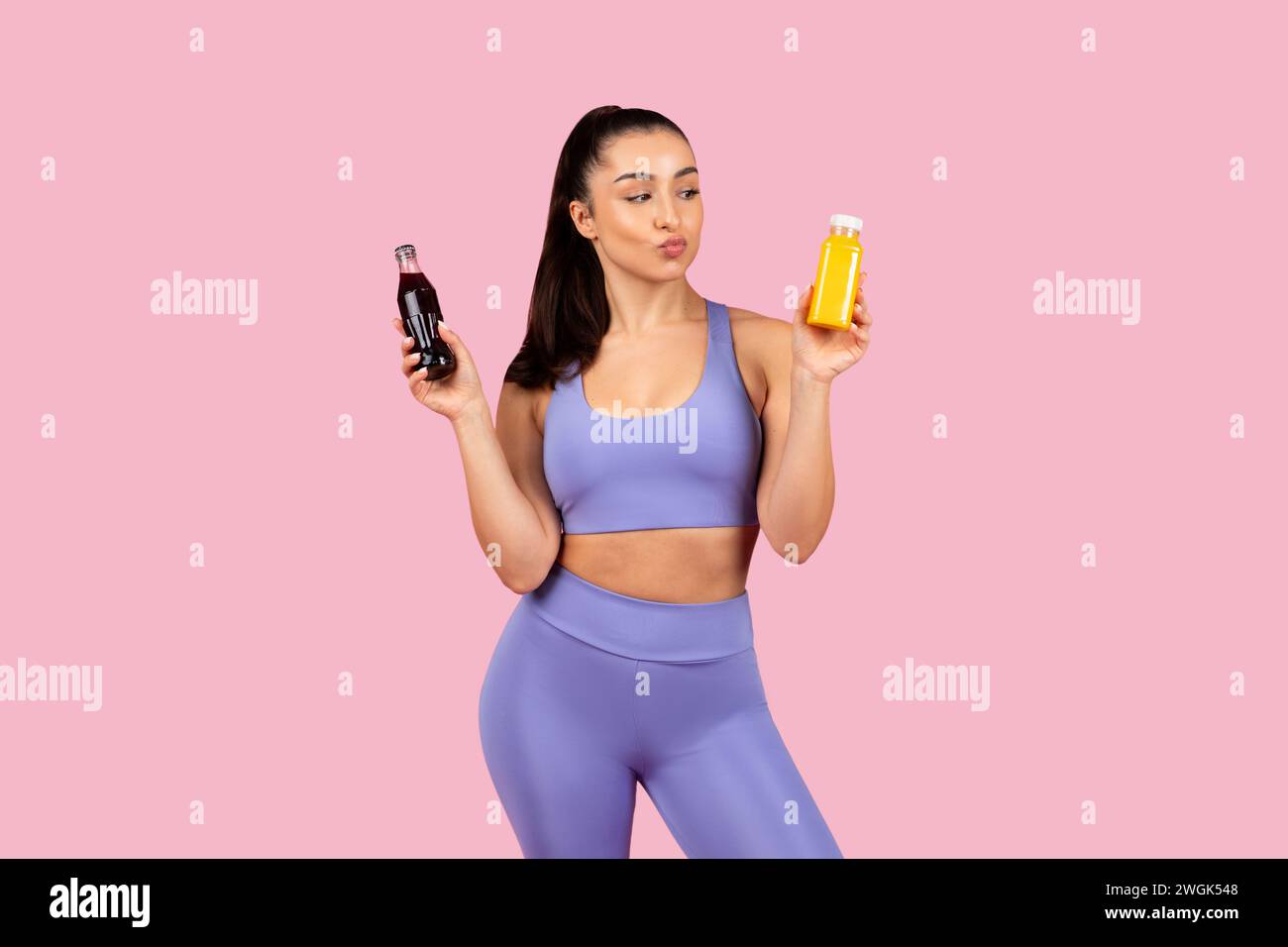 Fitness woman comparing drinks against pink background Stock Photo - Alamy