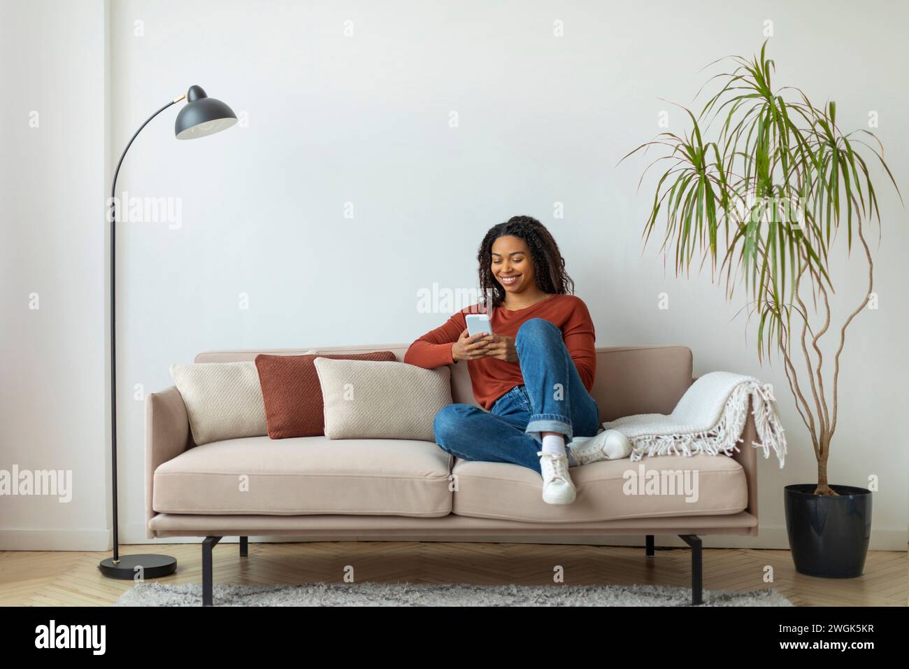 Happy Relaxed Black Woman With Smartphone Lounging On Couch At Home Stock Photo - Alamy