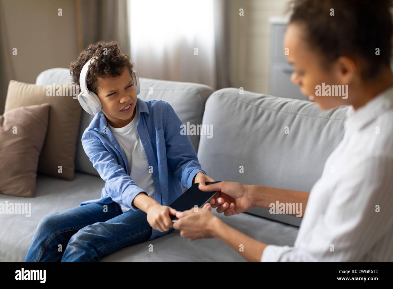Mother taking tablet from reluctant child with headphones Stock Photo ...