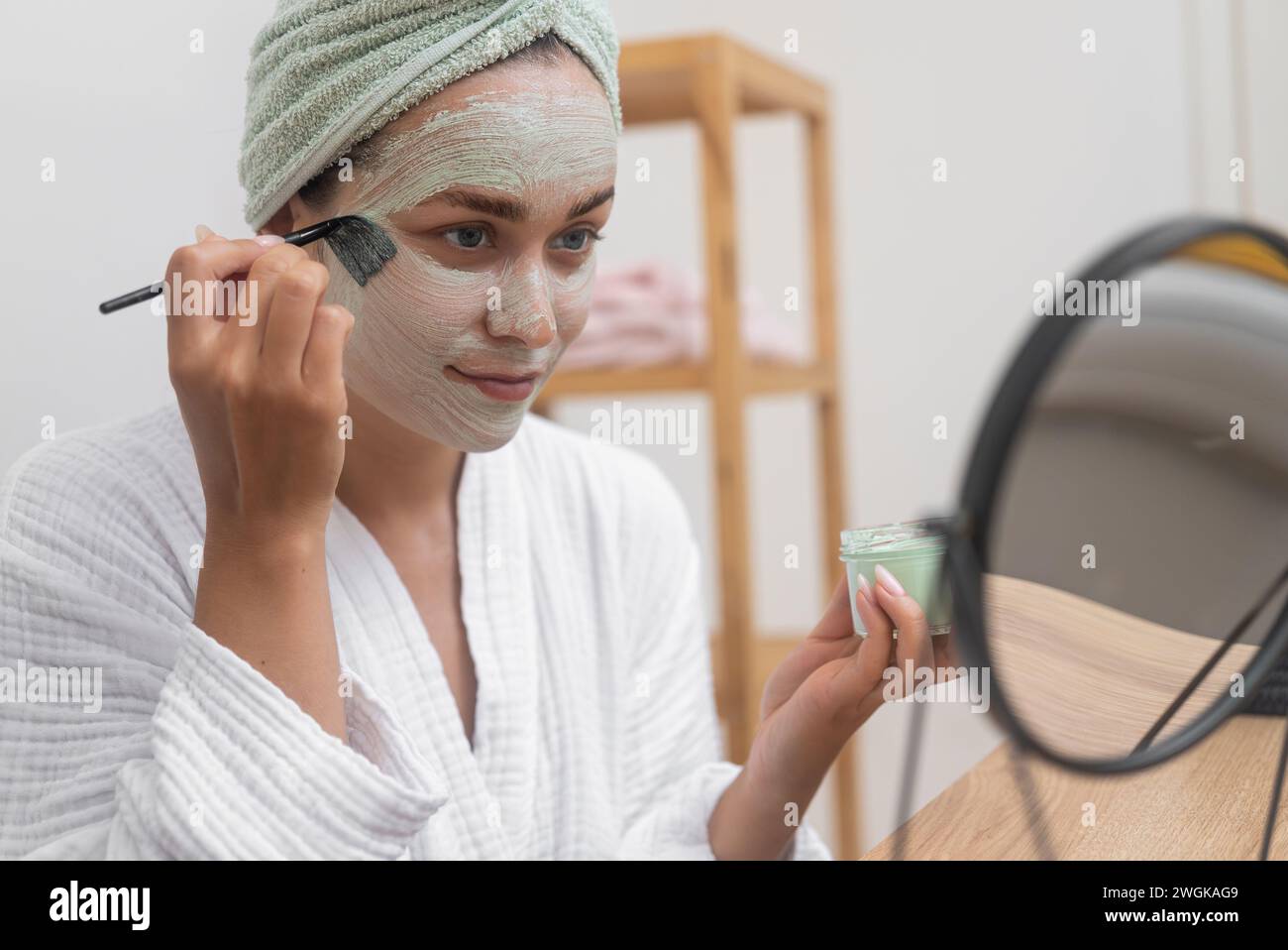 Towel-draped, she applies a facial mask for anti-aging, moisture, and ...